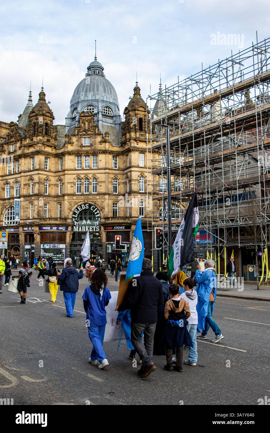 A group of people crosses a street in front of Leeds City Markets, some ...