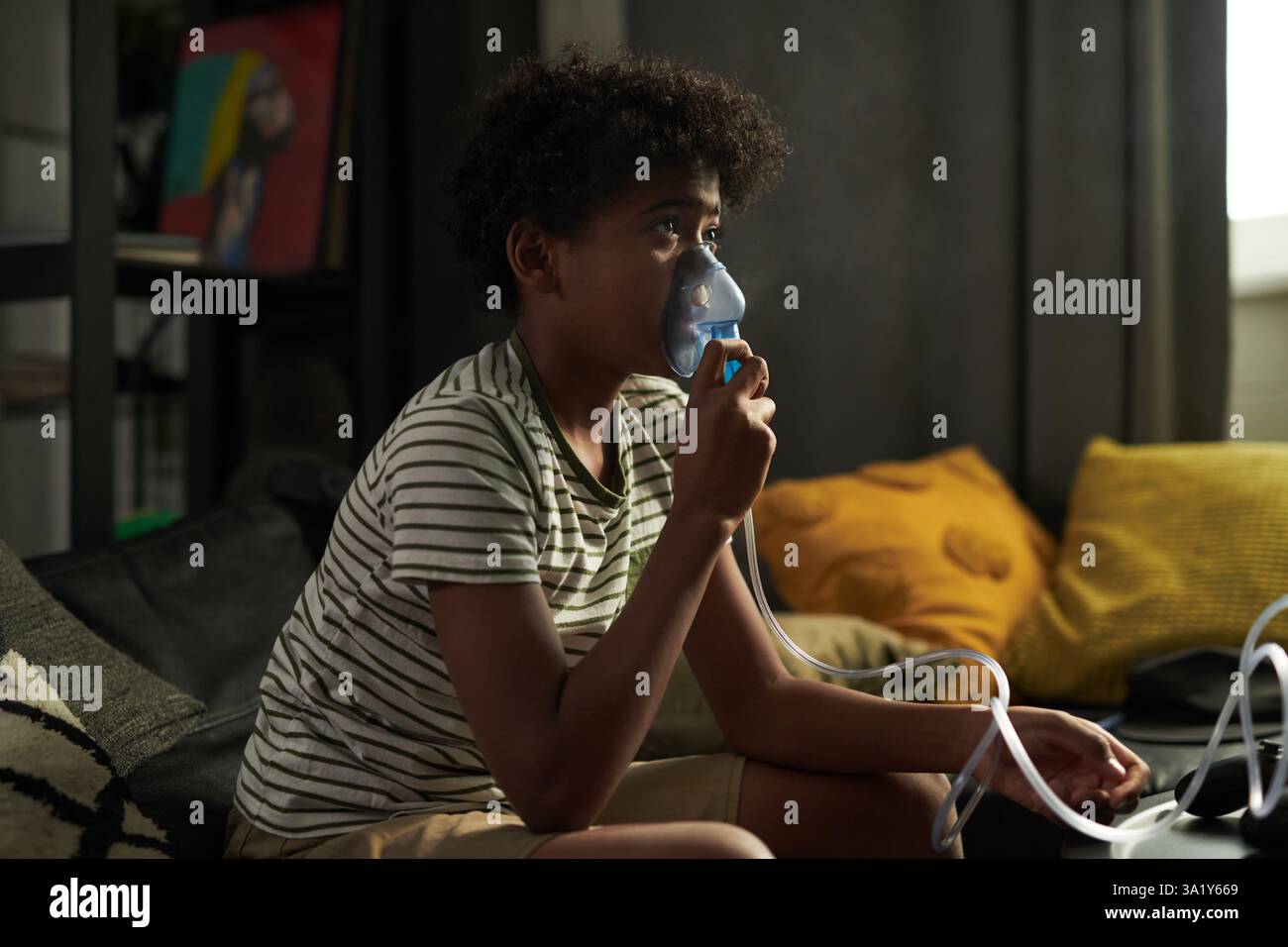 Side view of youthful boy with asthma inhaling fumes from nebulizer and ...