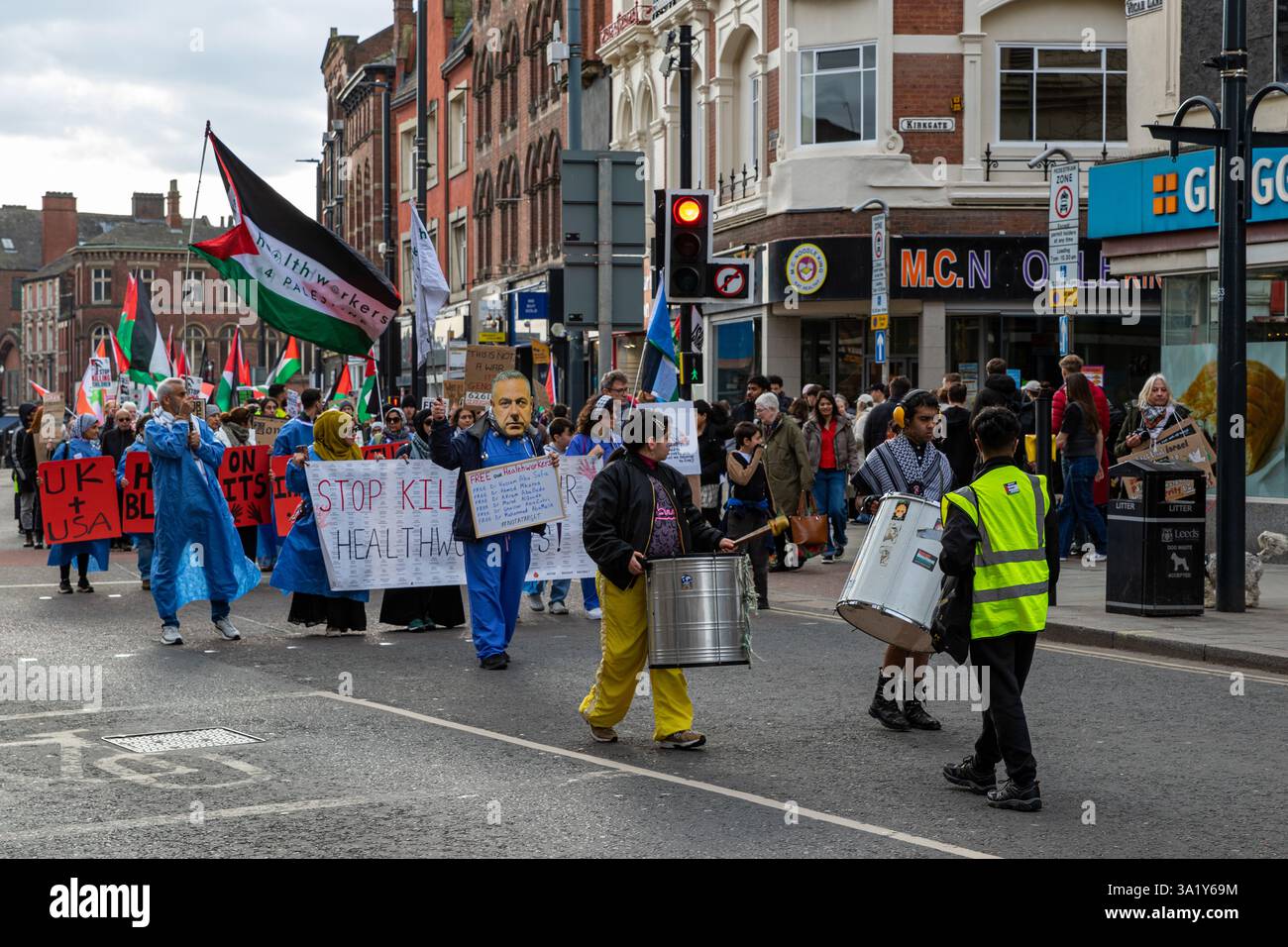 A street-level view shows a daytime protest march with signs ...