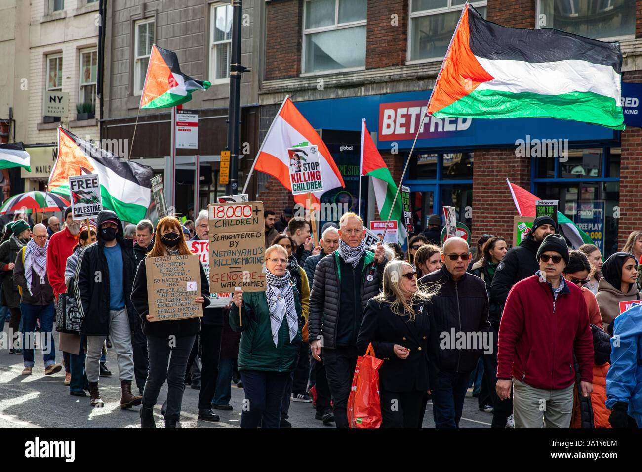 A crowd marches in protest, holding Palestinian flags and signs with ...