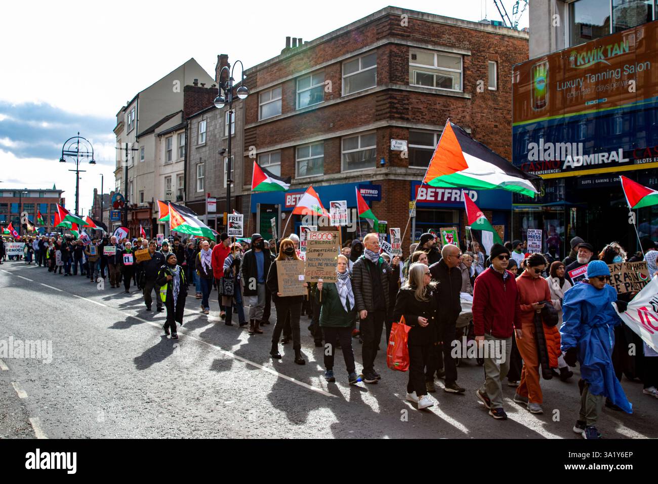 A street-level view of a daytime protest march. People are carrying ...