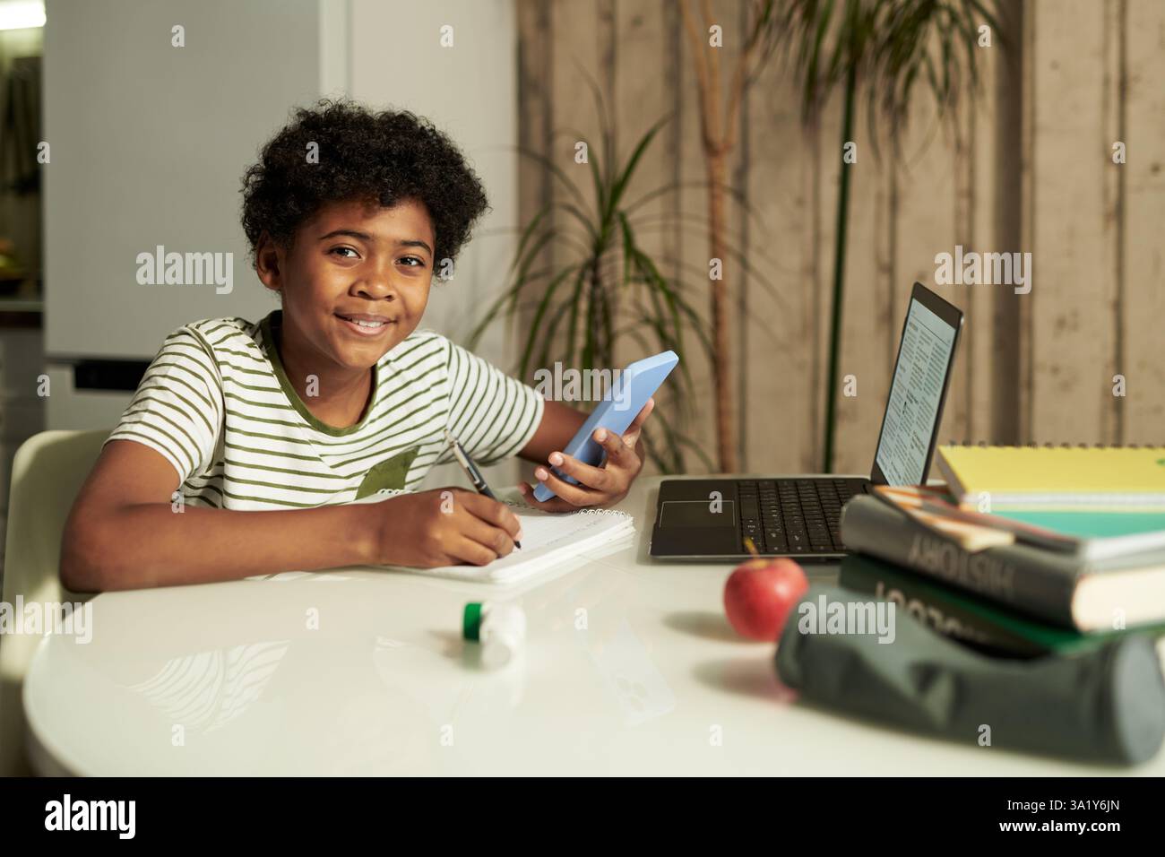 Cute smiling boy in t-shirt looking at camera while using smartphone ...