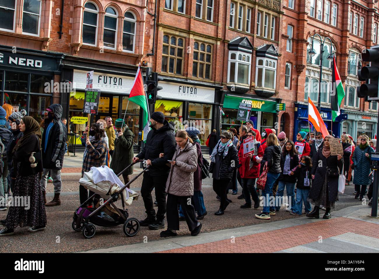 A crowd of people march along a city street holding flags and signs ...