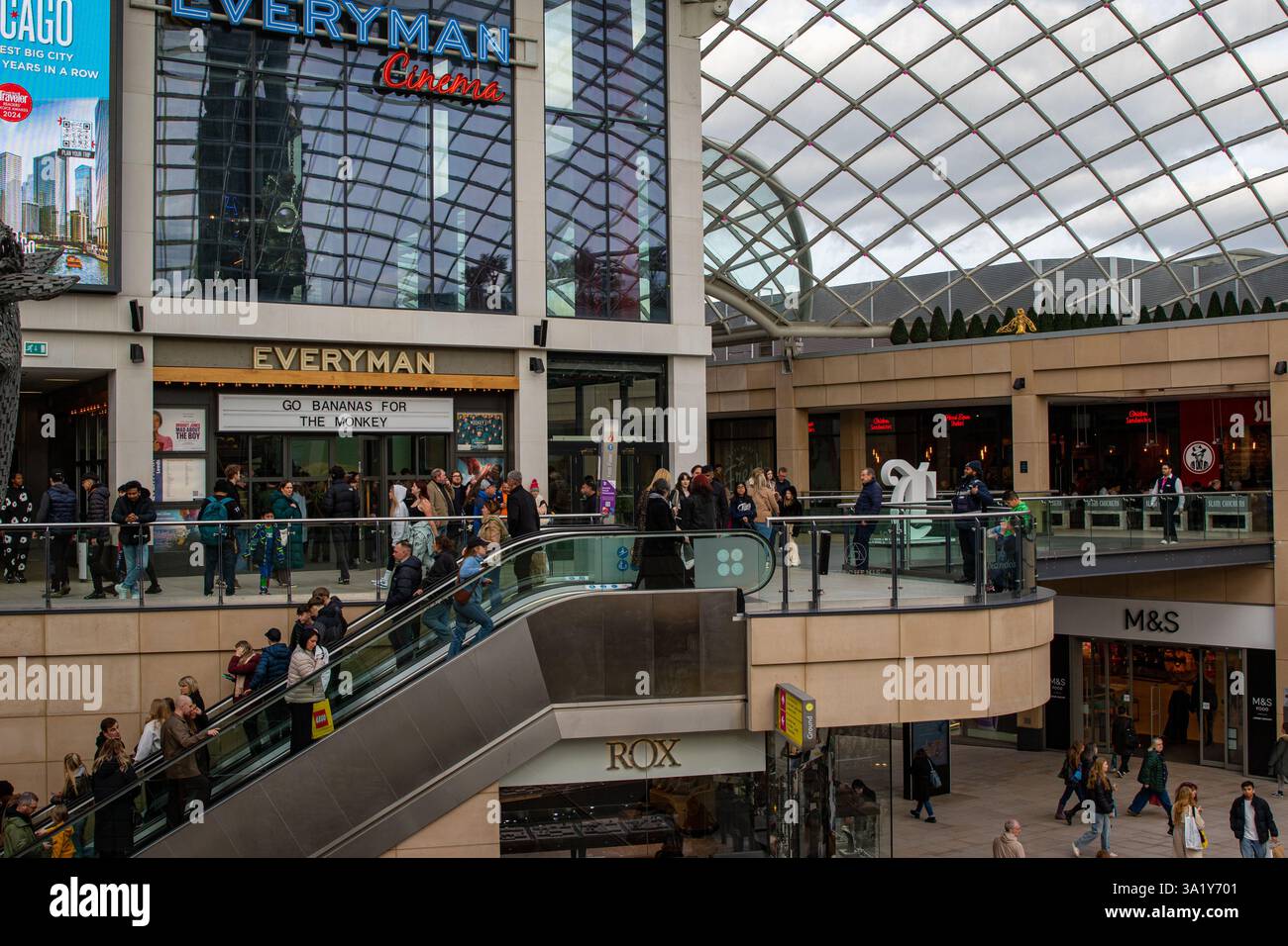 A multi-level shopping center features an escalator, the "Everyman ...