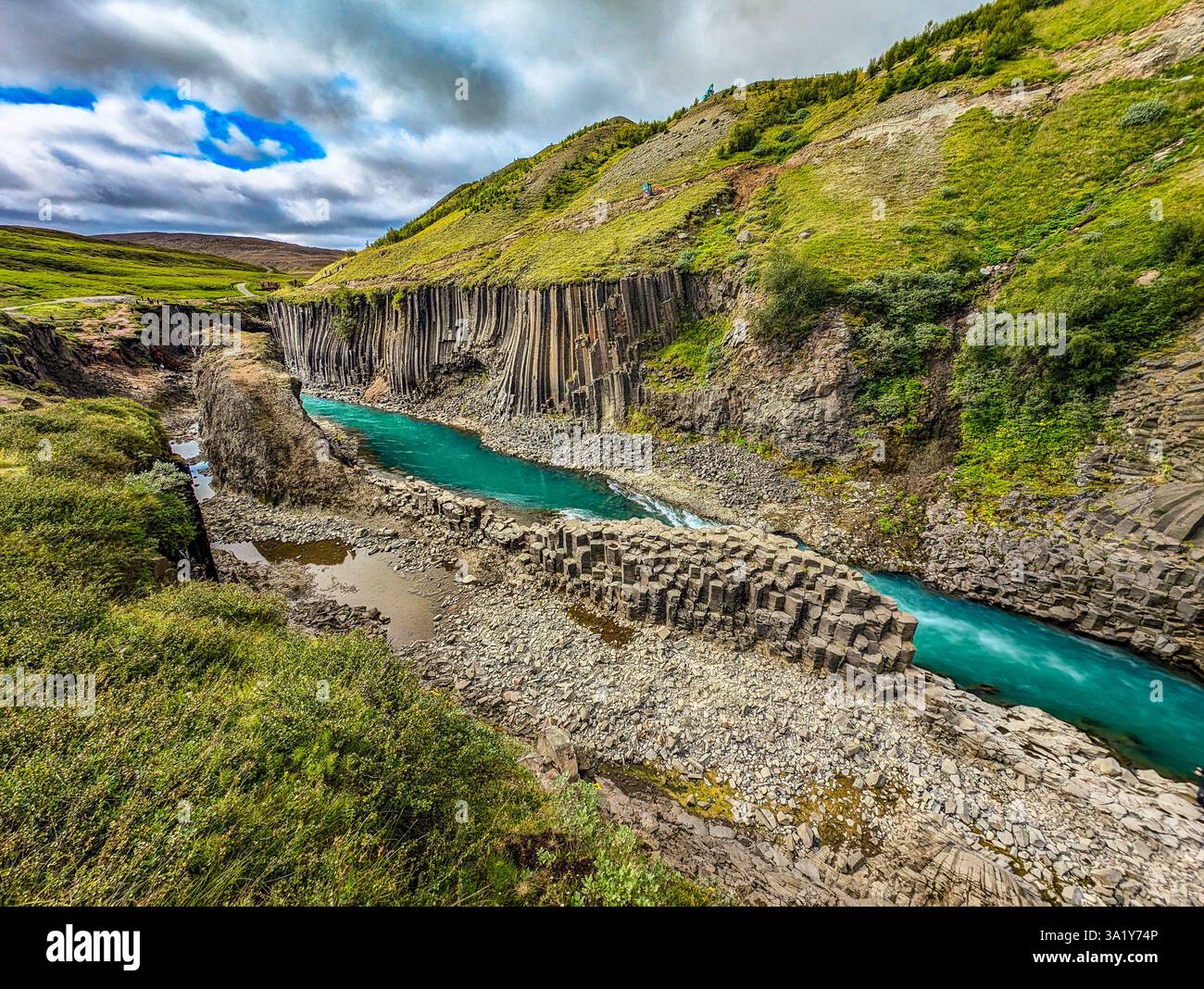 A scenic view of Studlagil Canyon in Iceland with basalt columns and a turquoise river flowing ...