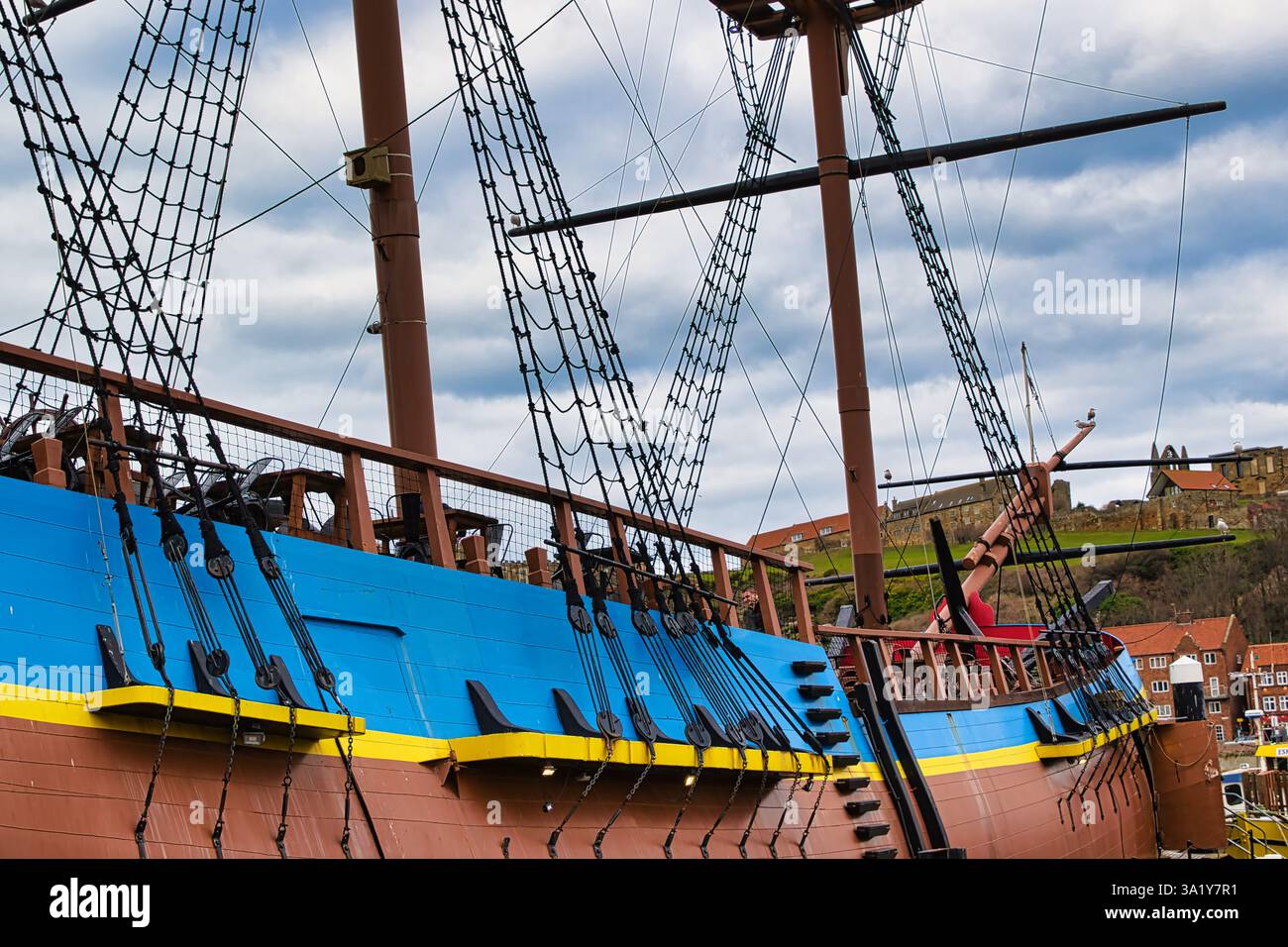 Detail of a tall ship's hull, masts, and rigging against a cloudy sky ...