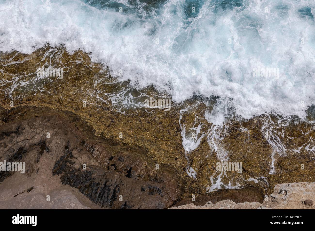Waves crashing against rocky shoreline of Atlantic Ocean on Gran Canaria, foamy water swirling ...