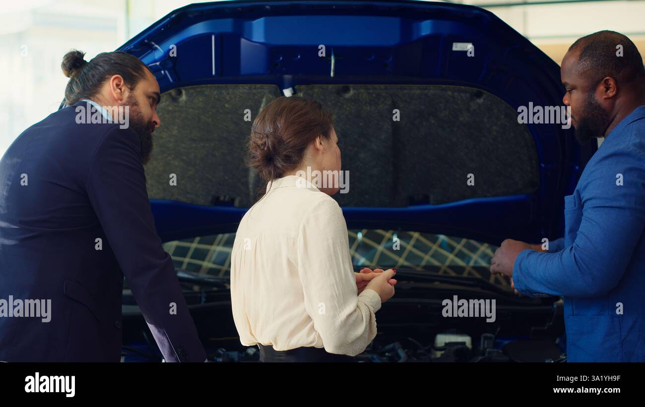 Friendly car salesman showing components under car hood to customers ...