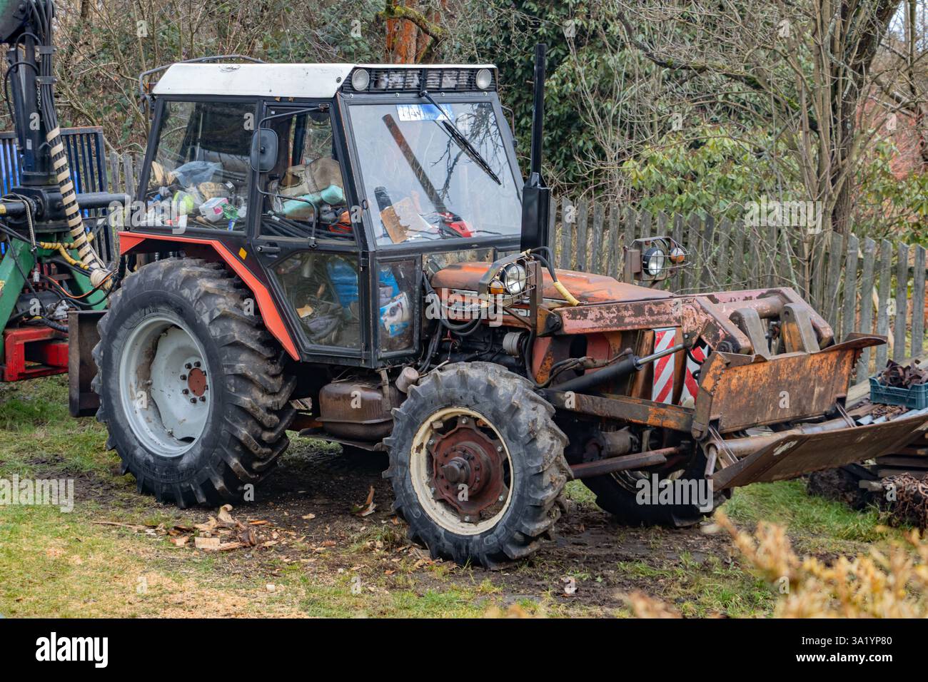 A tractor with a cabin full of junk stands in the yard of a family farm ...