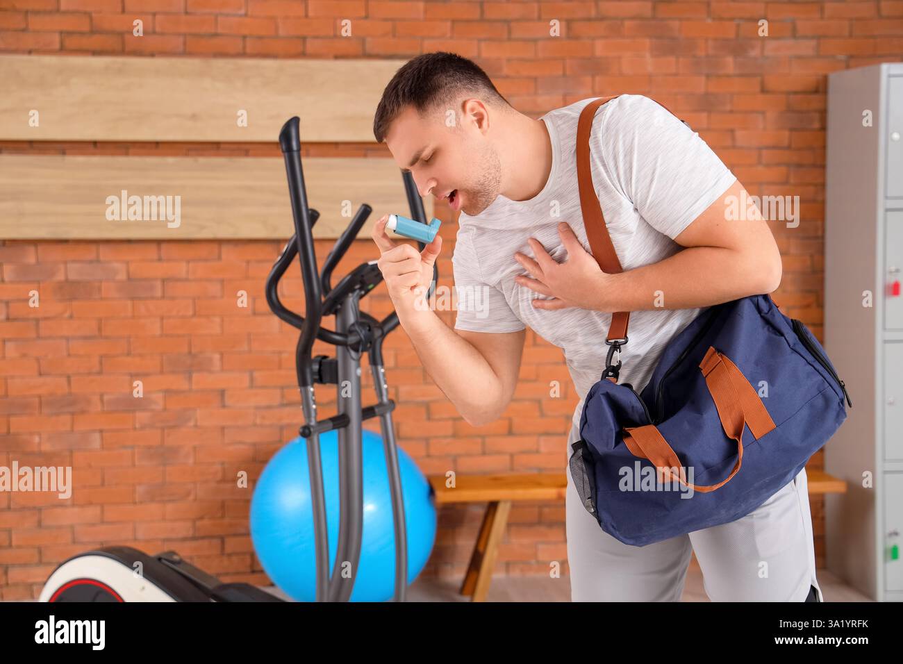 Sporty young man with bag using inhaler in gym Stock Photo - Alamy