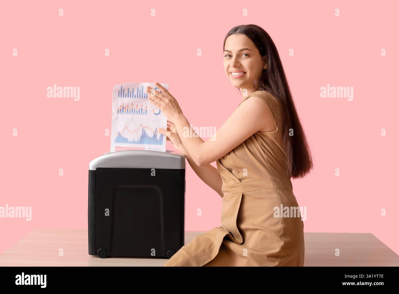 Happy young woman destroying documents using shredder on table against ...