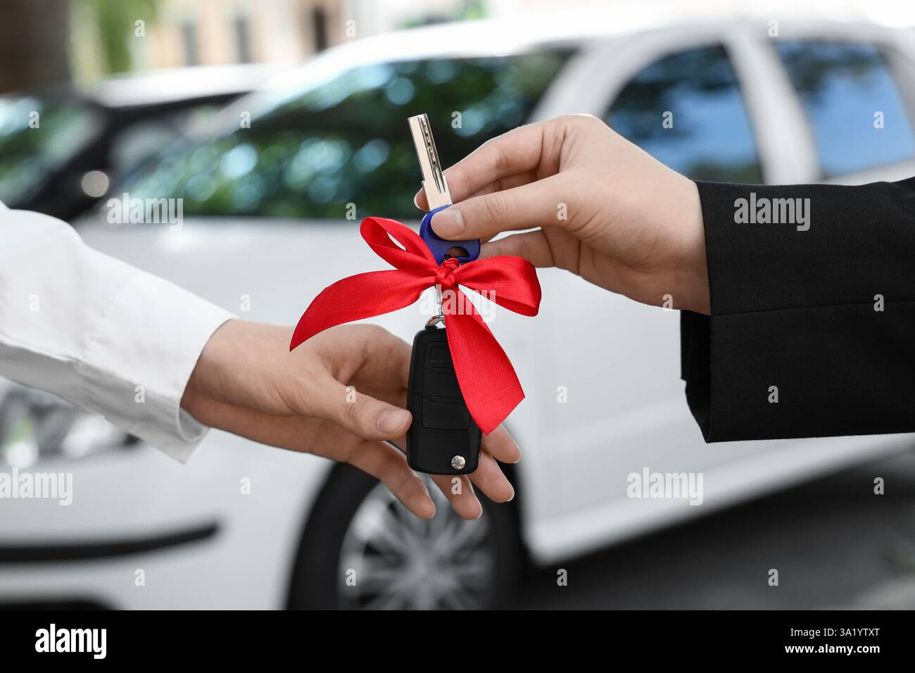 Woman giving gift keys of automobile to new owner in car showroom ...