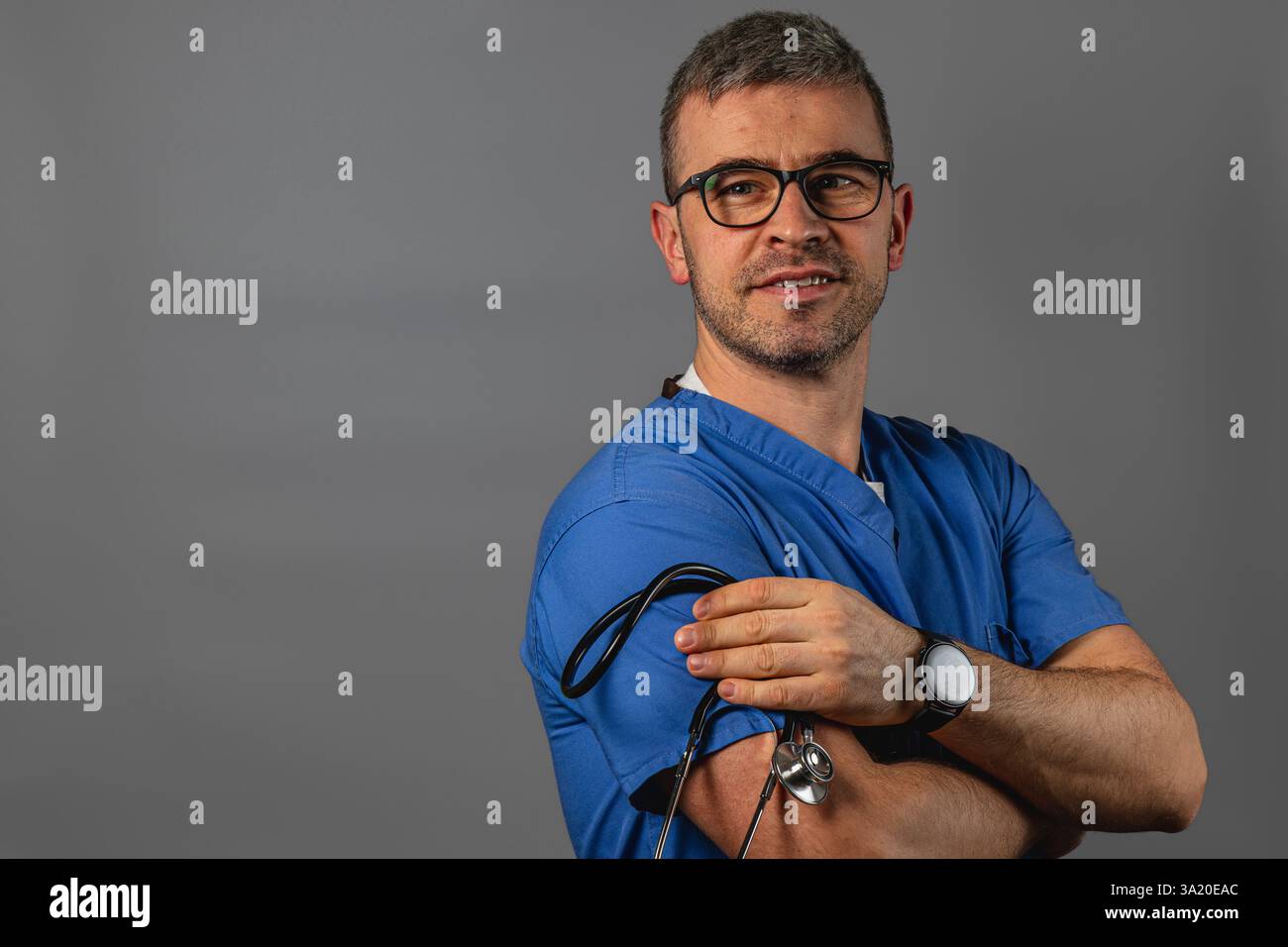 A man in blue scrubs stands confidently with a stethoscope draped over ...