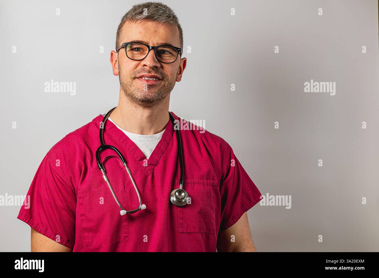 A healthcare worker wearing red scrubs and glasses stands confidently ...