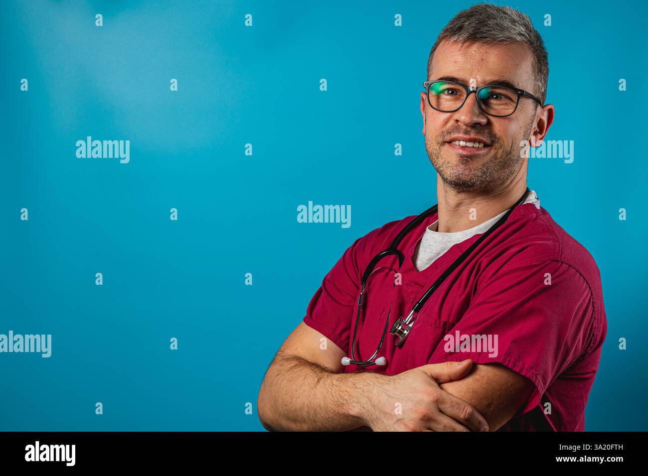 A healthcare professional wearing red scrubs and glasses stands ...