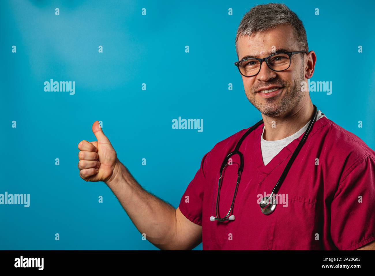 A healthcare worker dressed in scrubs smiles and gives a thumbs up ...