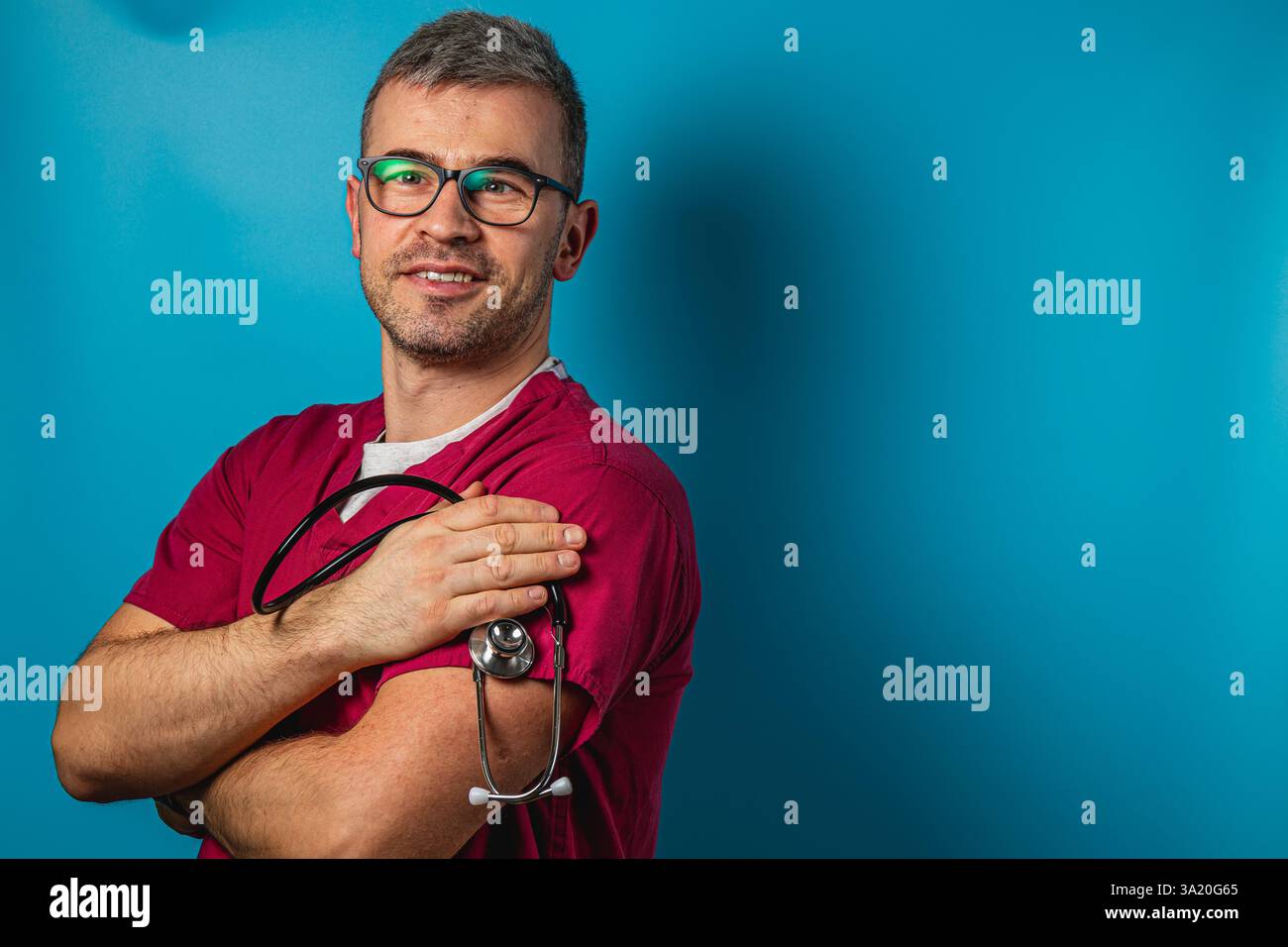 A male healthcare worker wearing pink scrubs and glasses stands ...