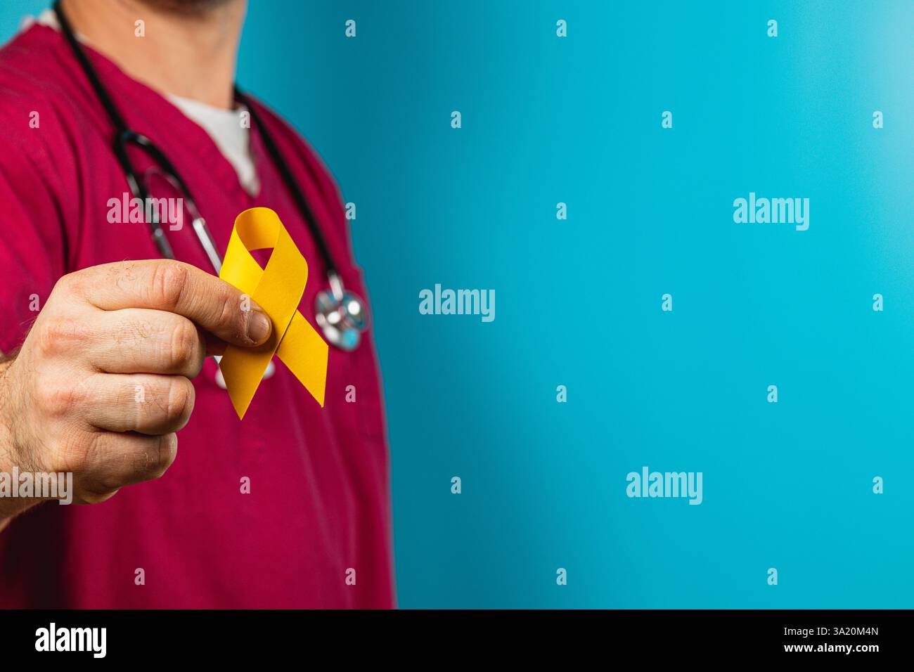 A healthcare professional in scrubs displays a yellow awareness ribbon ...