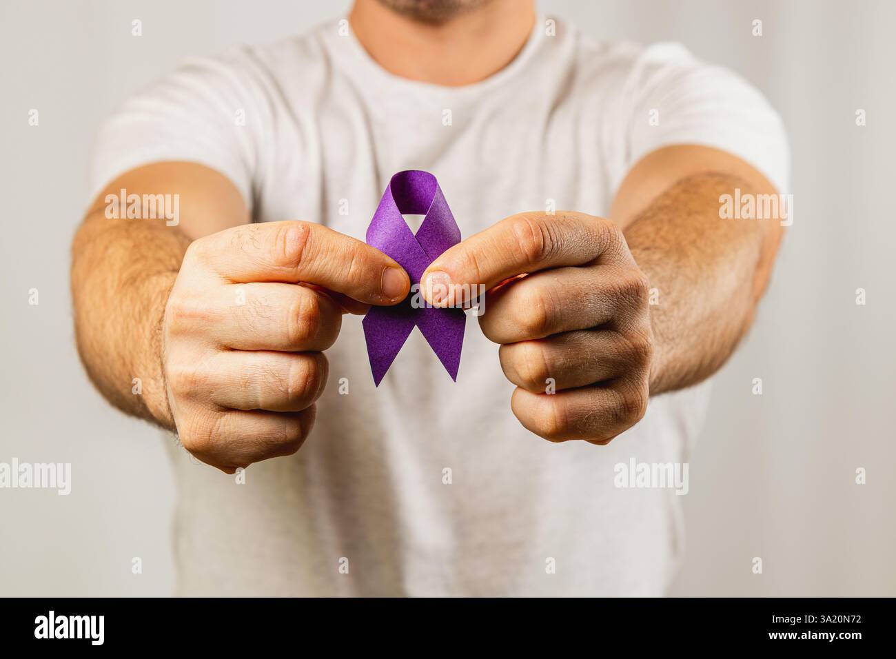 A person holds a purple ribbon between their hands, demonstrating ...