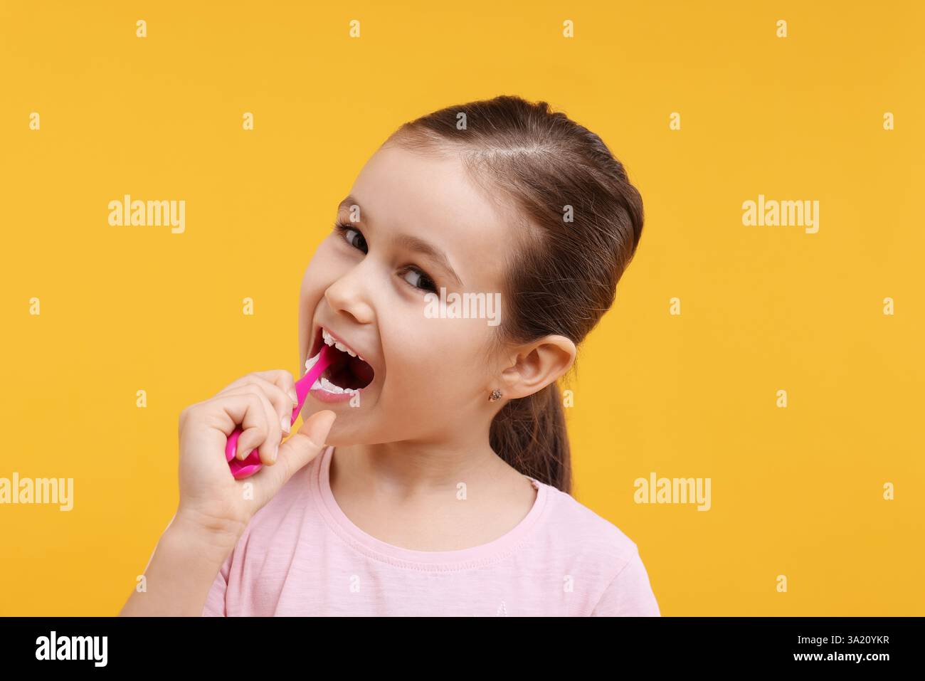 Cute girl brushing her teeth on orange background Stock Photo - Alamy