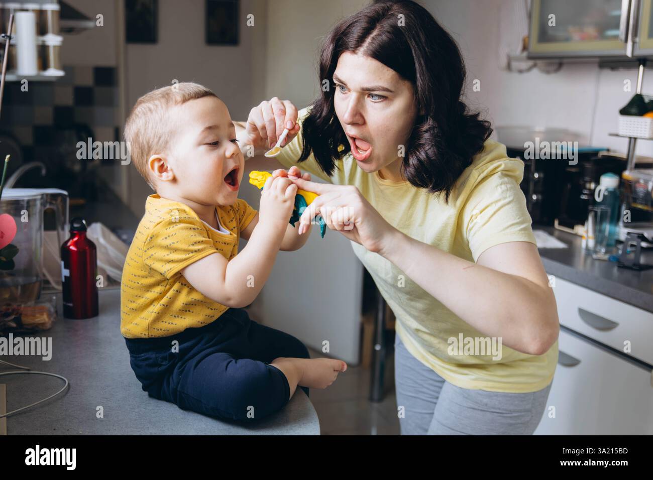 Mother feeding her son with a spoon in the kitchen, sharing a joyful ...