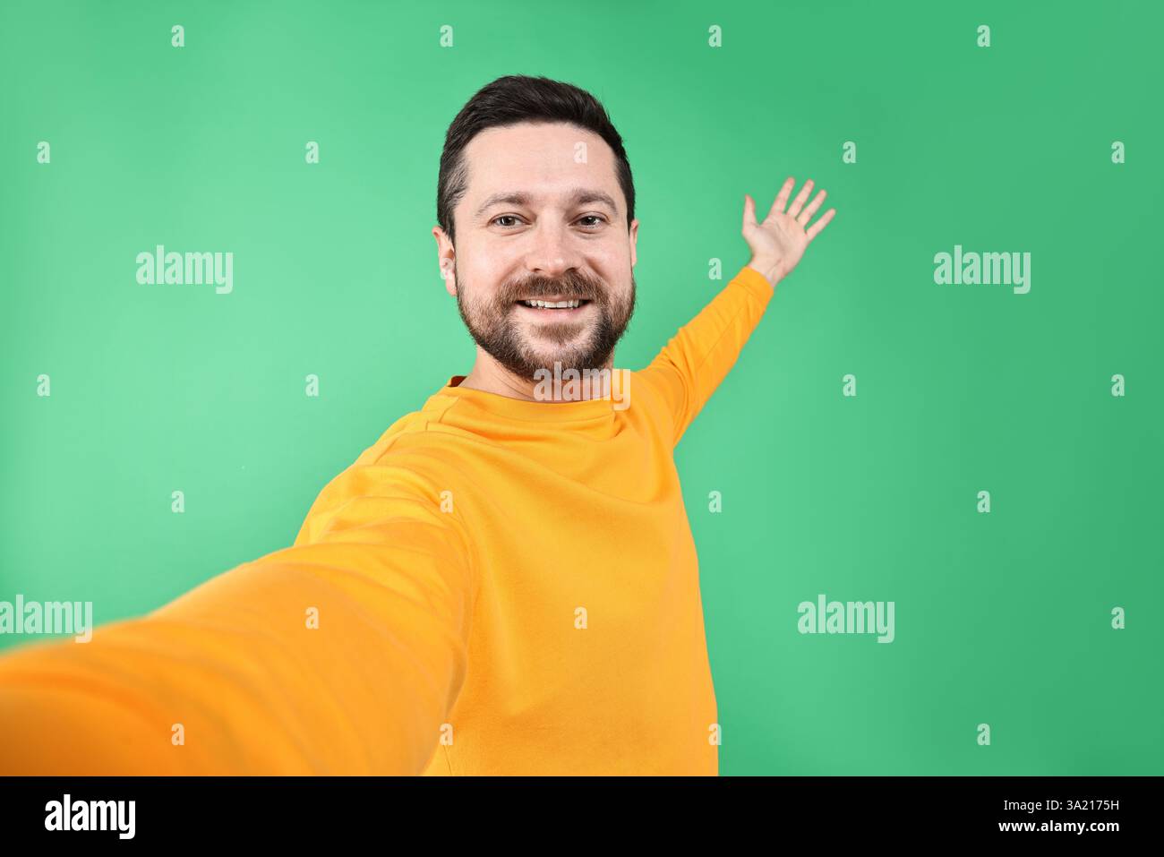Happy man welcoming friends or guests by video call on green background ...