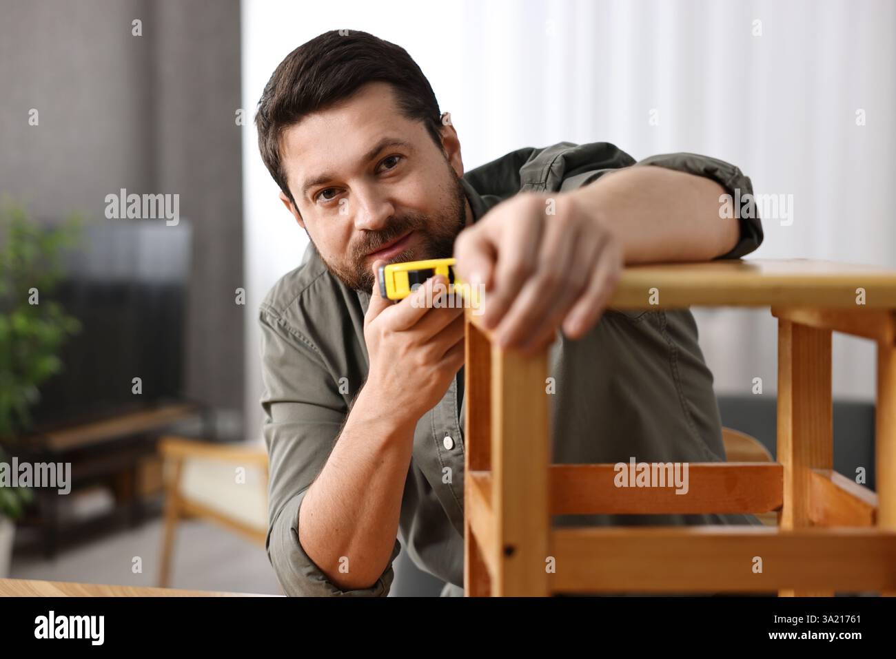 Man using tape measure while repairing wooden stool at home Stock Photo ...