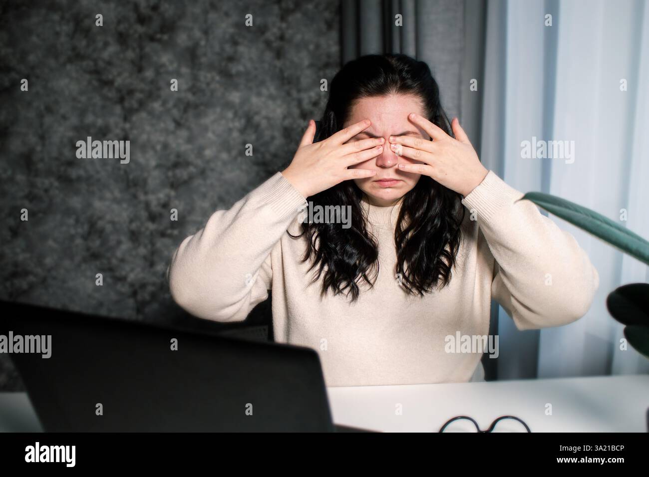 Woman working from home office sitting with laptop rubbing tired eyes ...