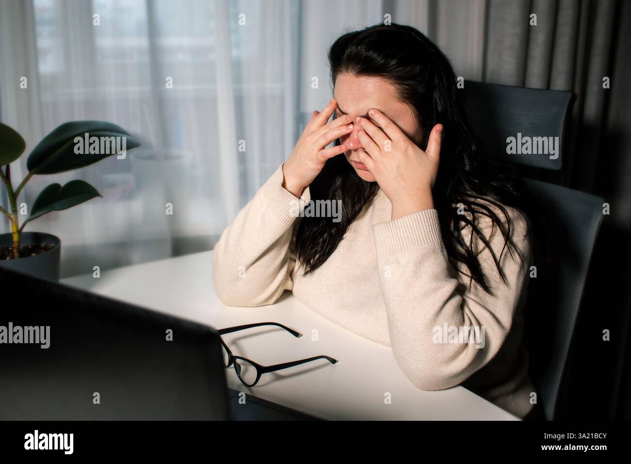 Woman working from home office sitting with laptop rubbing tired eyes ...