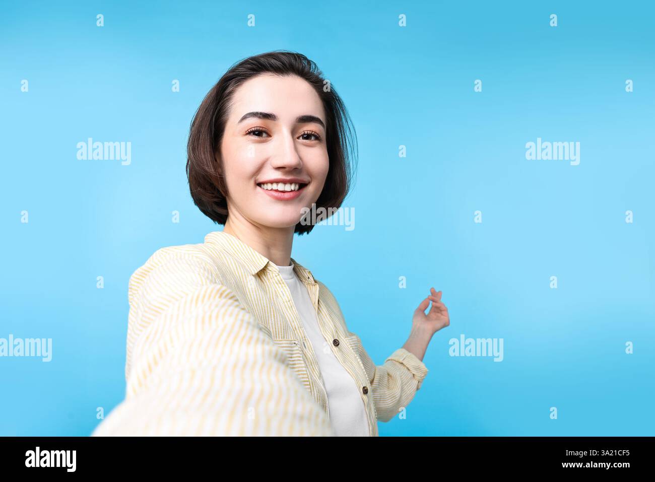 Cheerful woman welcoming friends or guests via video call on light blue ...