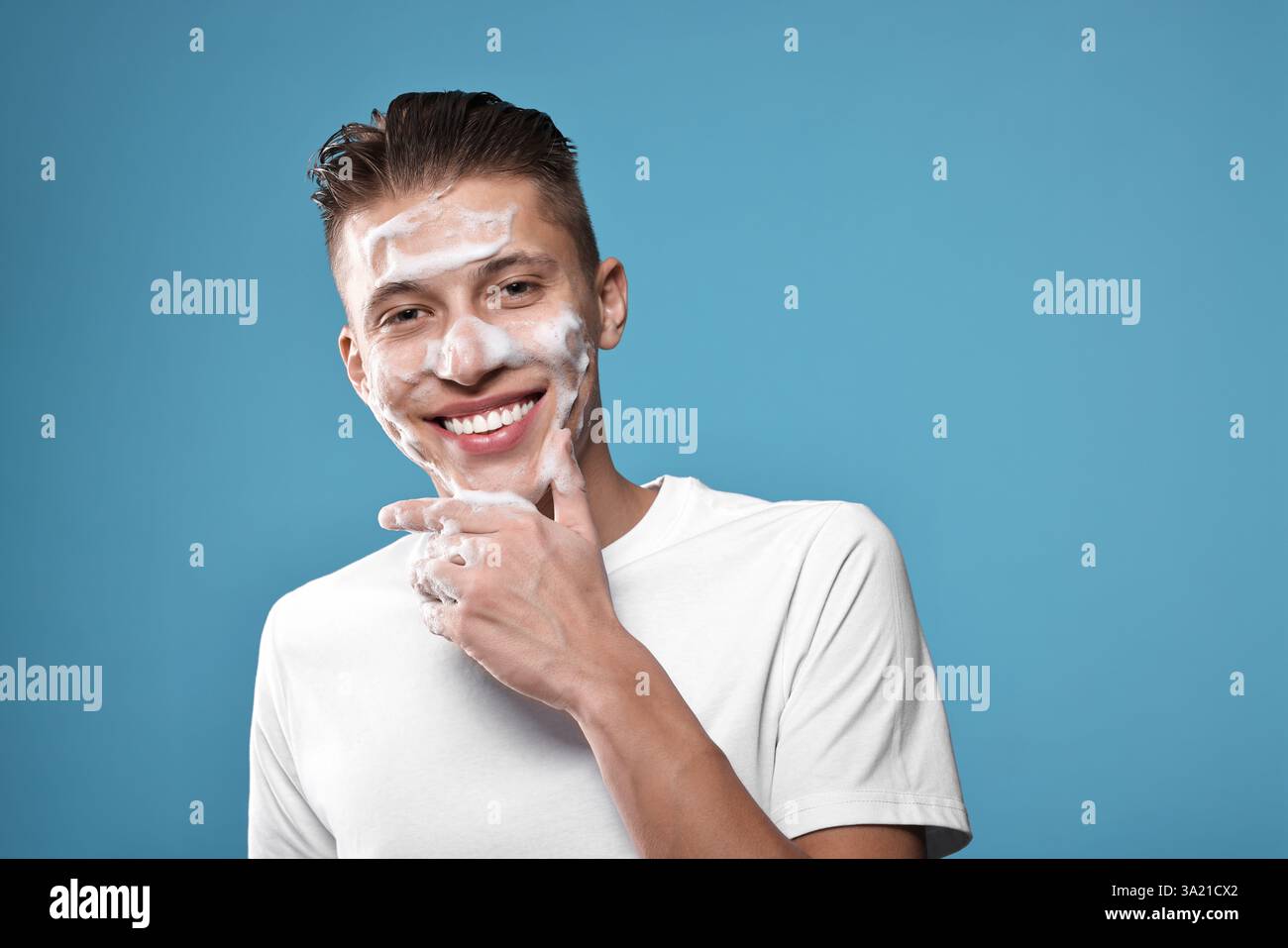 Smiling man with cleansing foam on his face against blue background. Washing routine Stock Photo ...