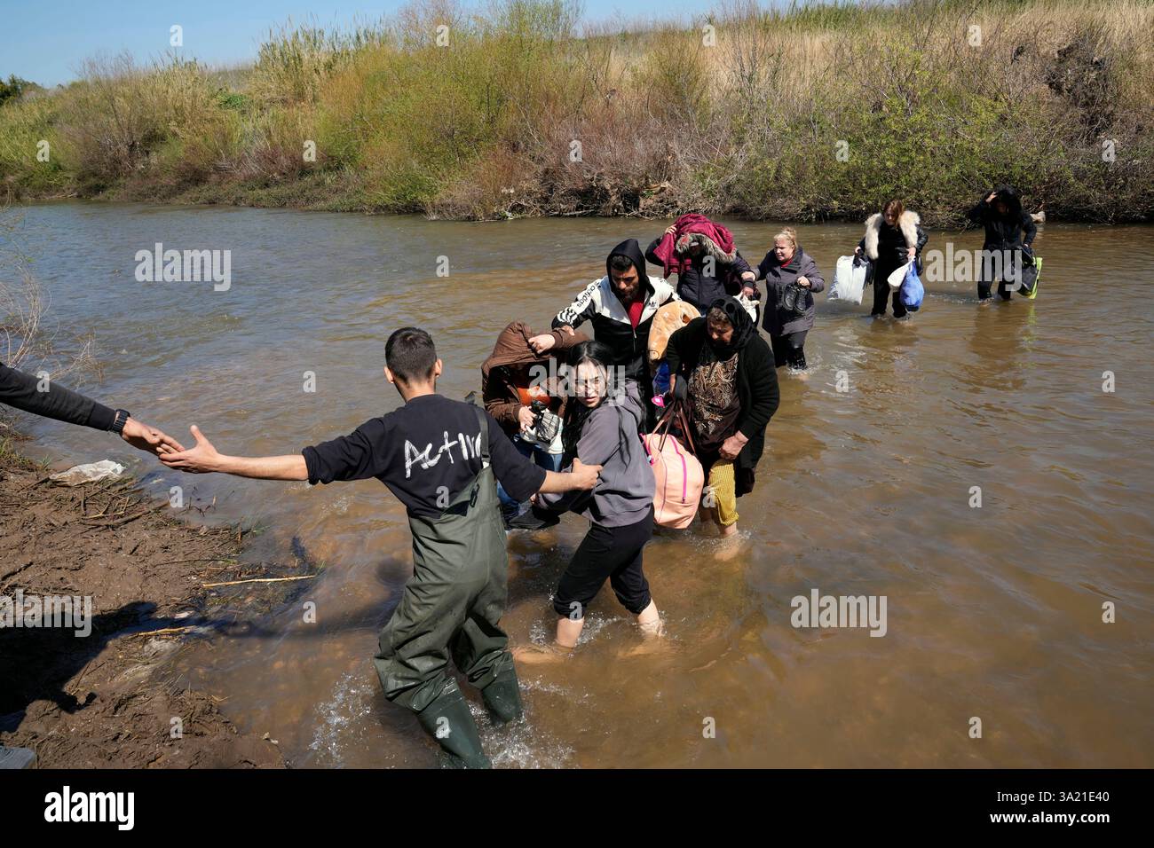 Syrian families cross a river marking the border between Syria and ...