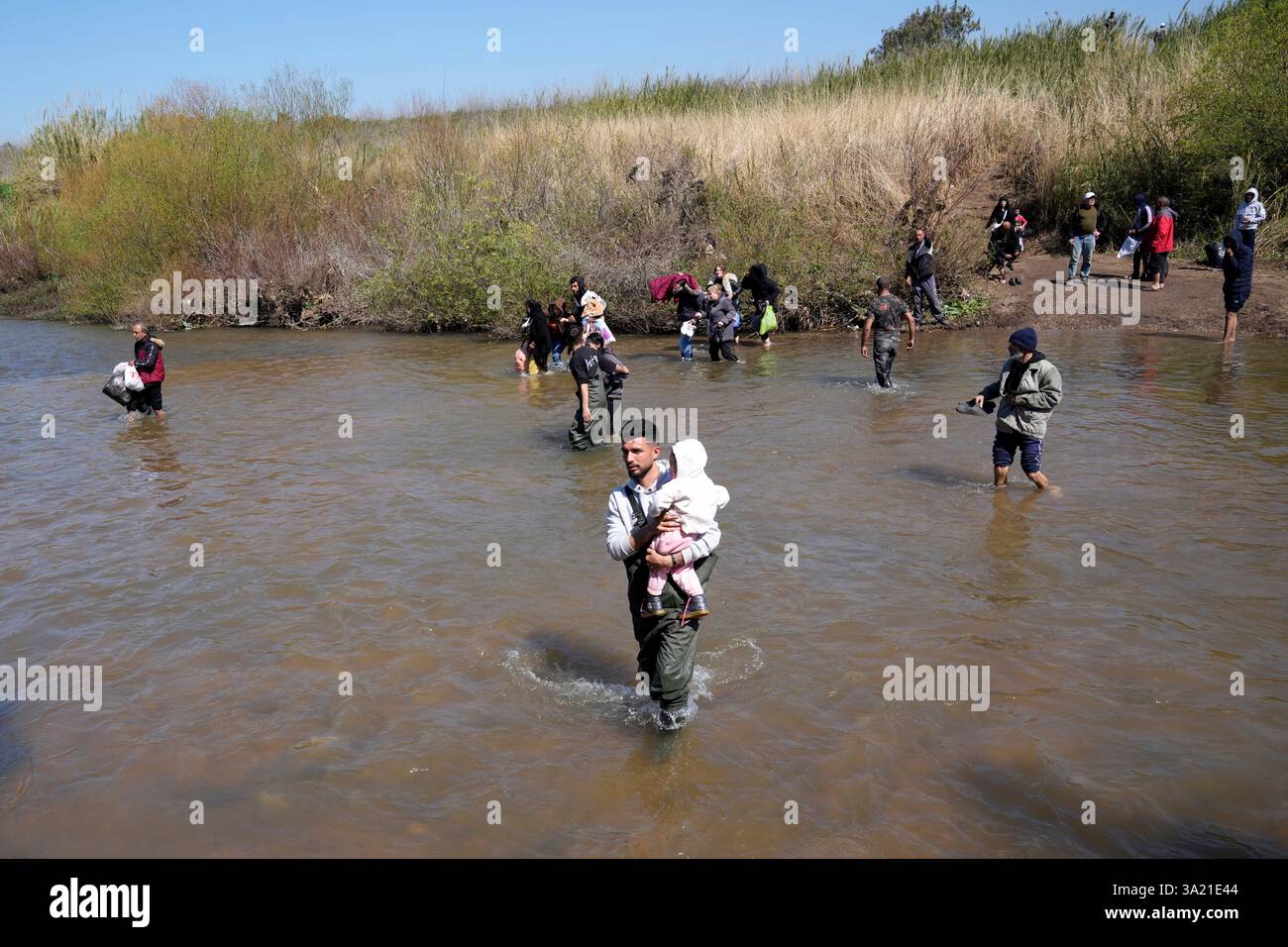 Syrian families cross a river marking the border between Syria and ...