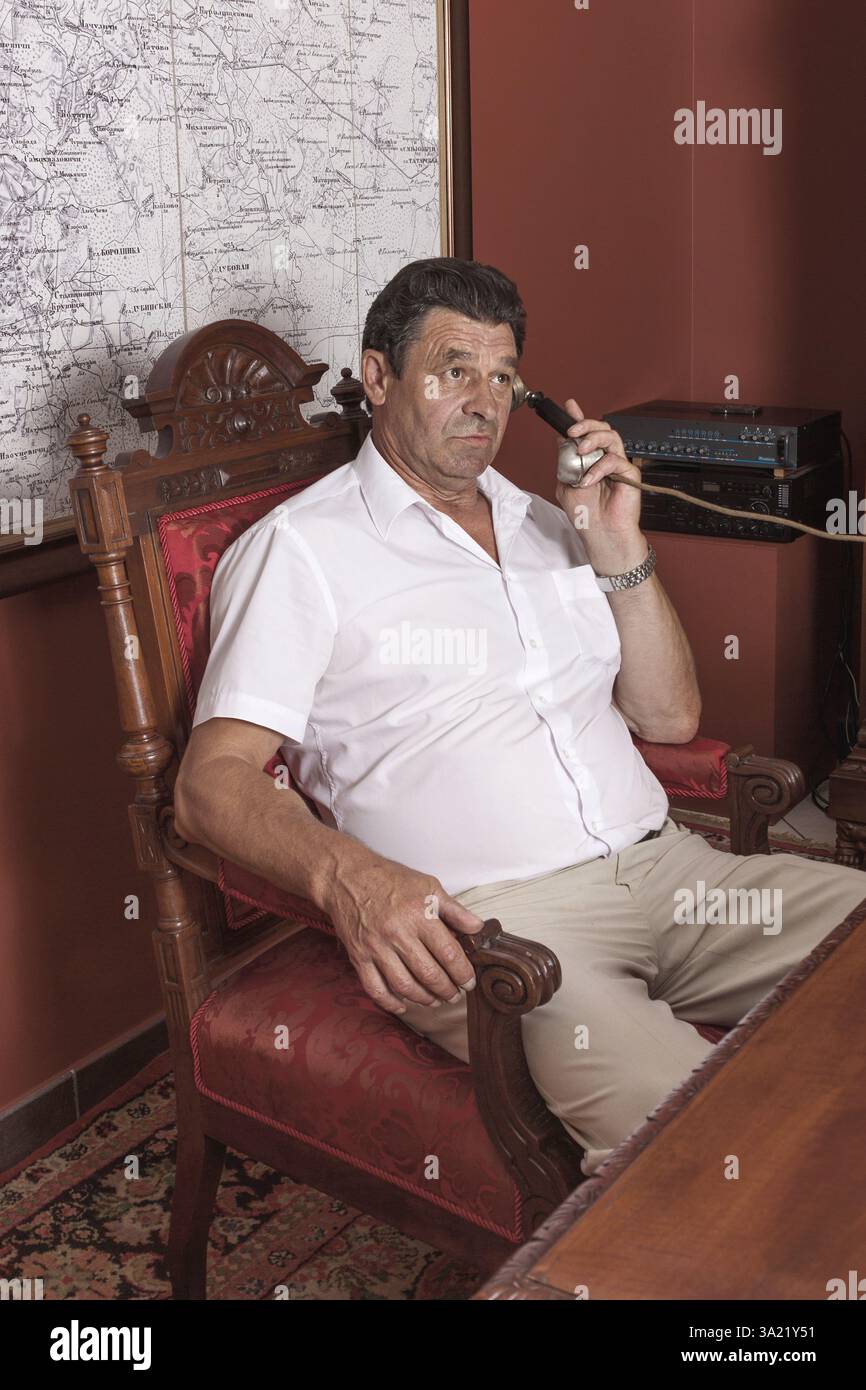 A man holding an important public position sits at a desk in his retro-elite office. He talks on ...