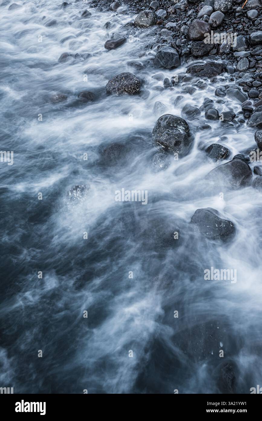 Waves gently crash against a rocky shoreline in Madeira, creating a ...