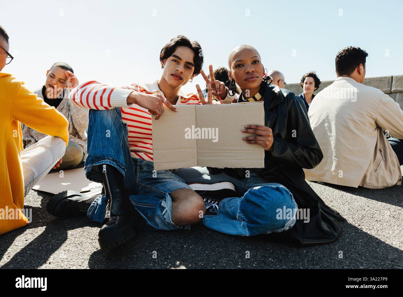 Two individuals sitting together at a outdoor protest, holding a blank ...