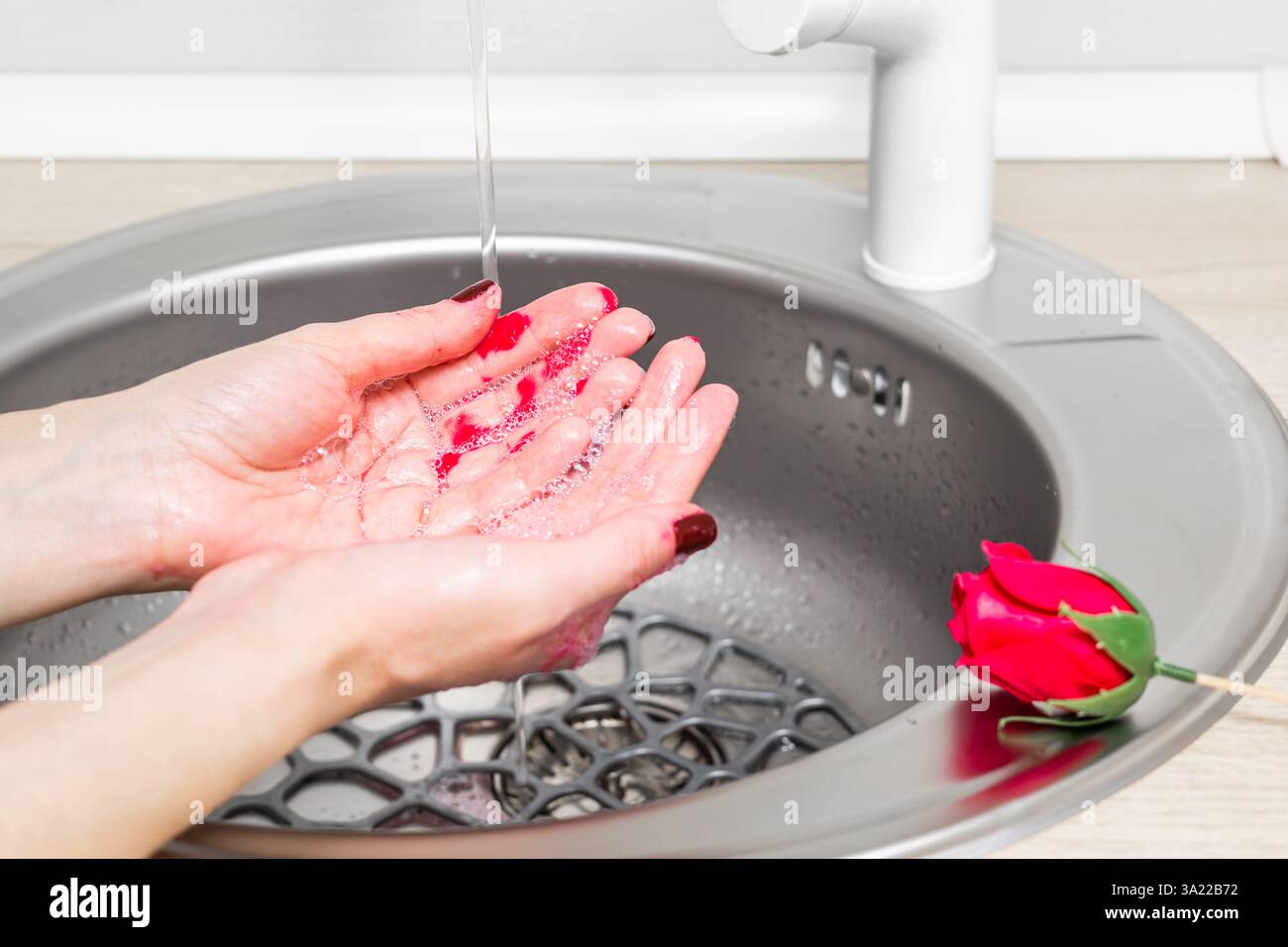 woman washes her hands with red soap. soap flower near the sink. woman ...