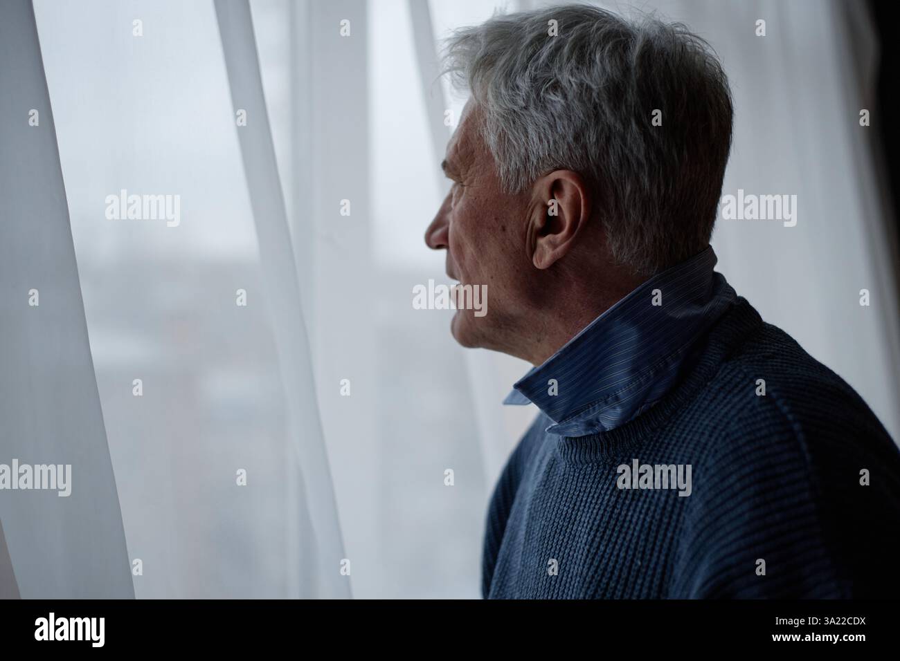 Elderly man with gray hair gazing out window with contemplative ...