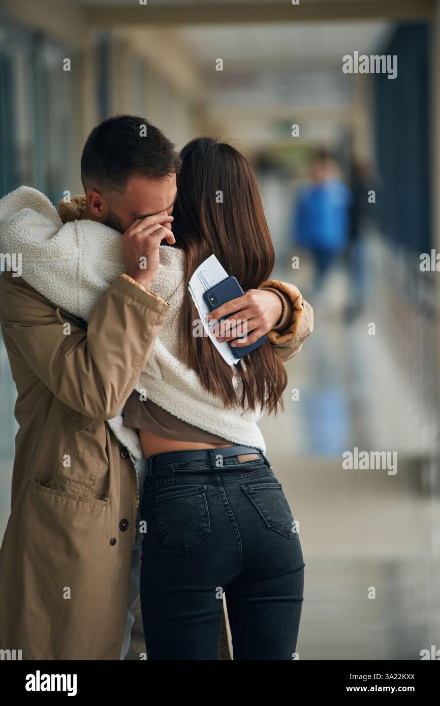 Man is crying, embracing, farewell. Couple are in the airport hall ...