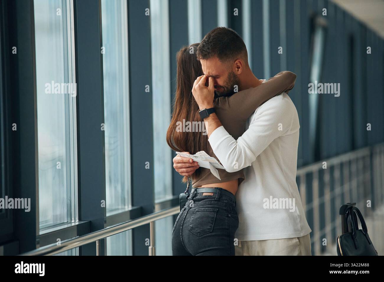 Man is crying, embracing, farewell. Couple are in the airport hall ...