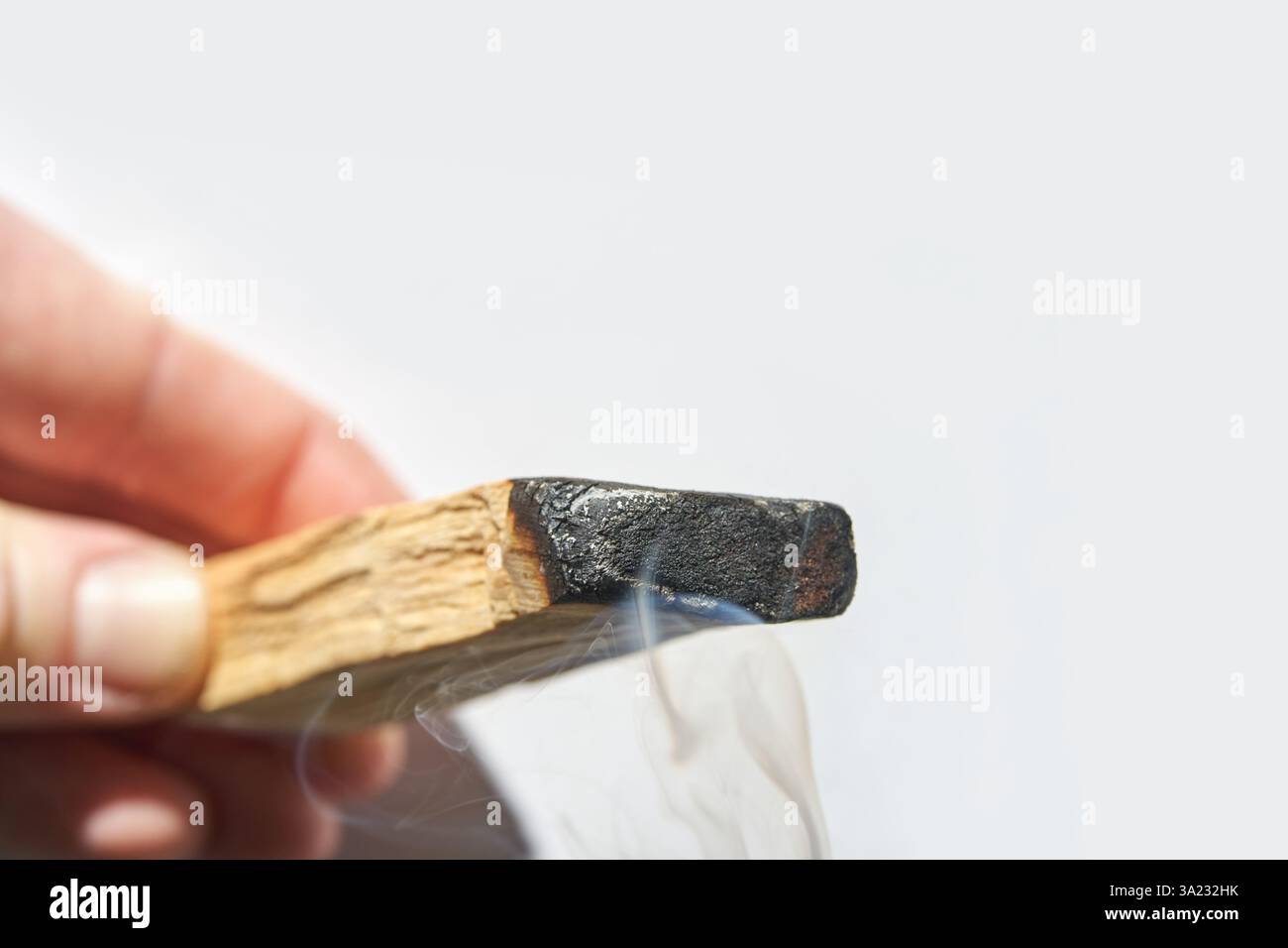 Hand holding smoldering palo santo stick with rising smoke against ...