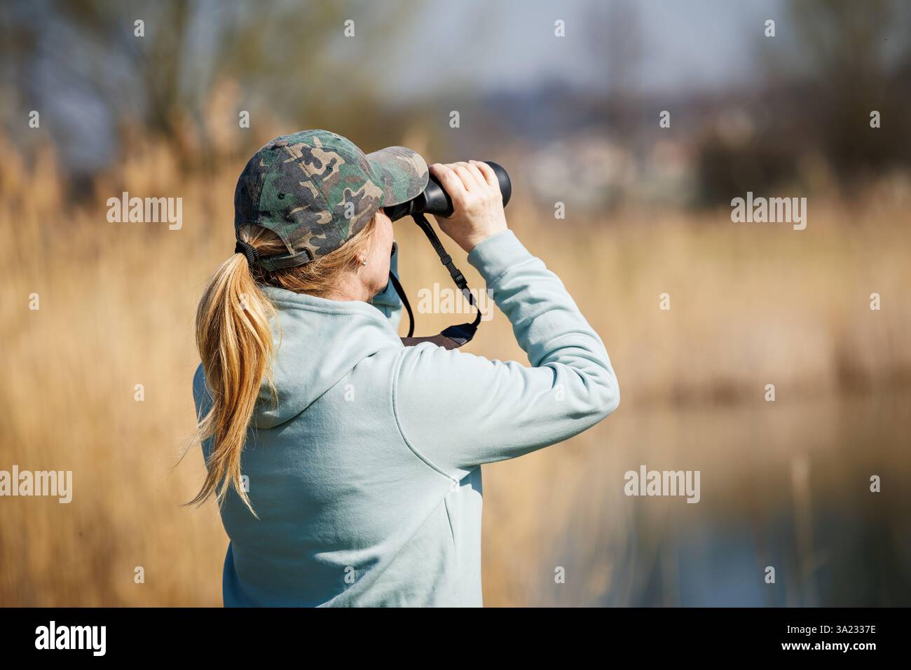 Woman explorer with binoculars watching birds and animals at lake ...