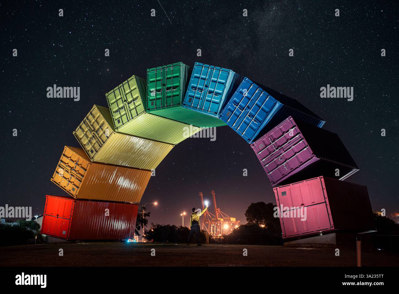 man with light standing under rainbow containers at night Stock Photo ...