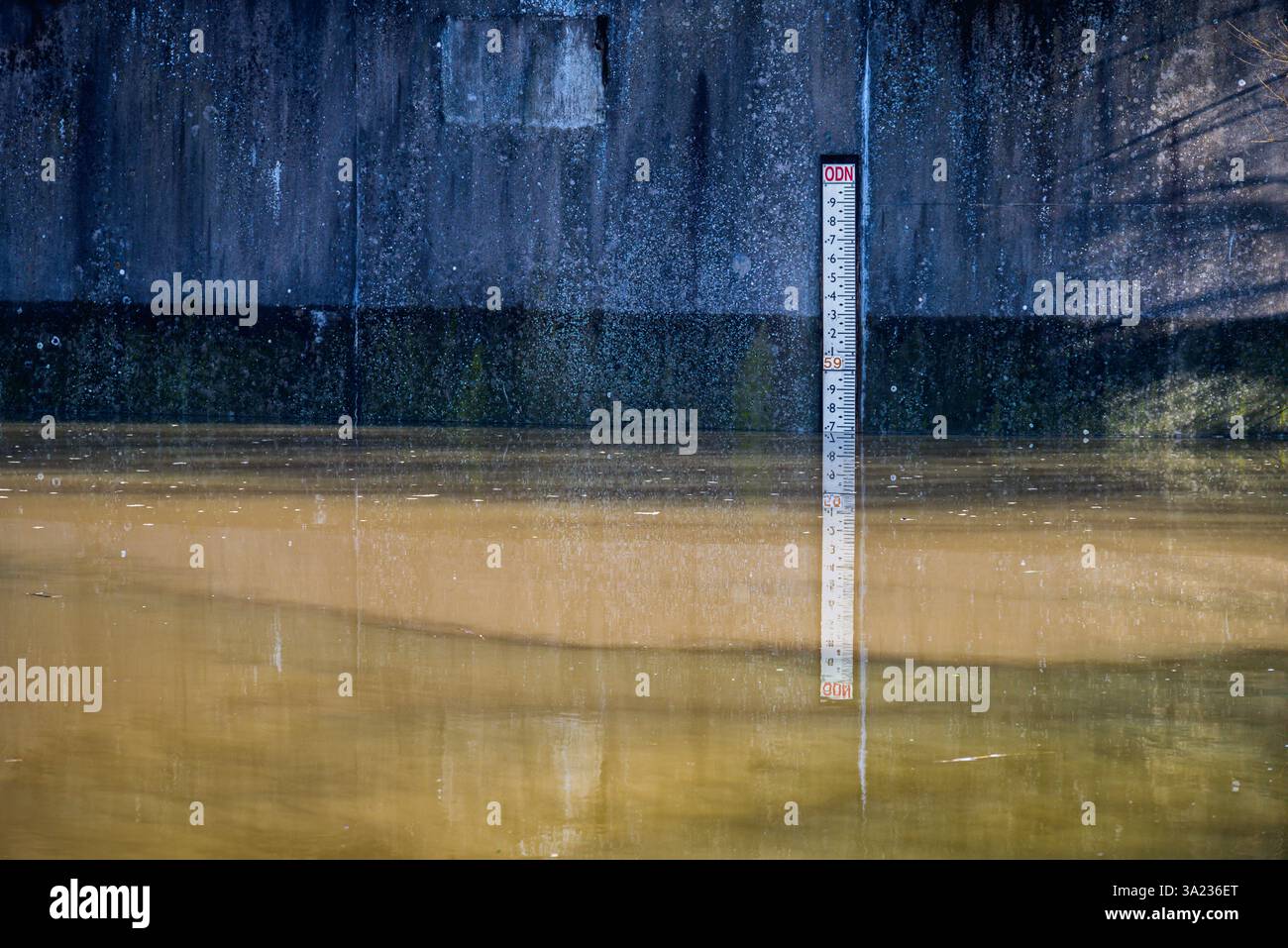 A water level ruler on the concrete dam wall is mirrored in the muddy ...