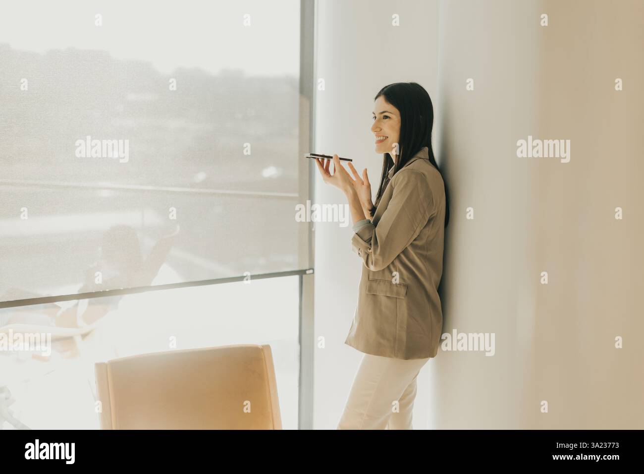 A young woman leans against a wall, smiling as she talks on the phone ...