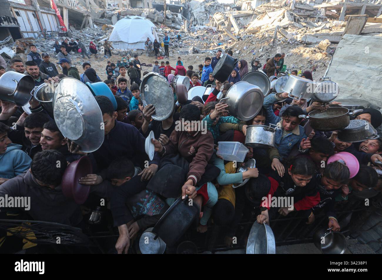 Displaced Palestinians queue to receive a share of food from a charity ...