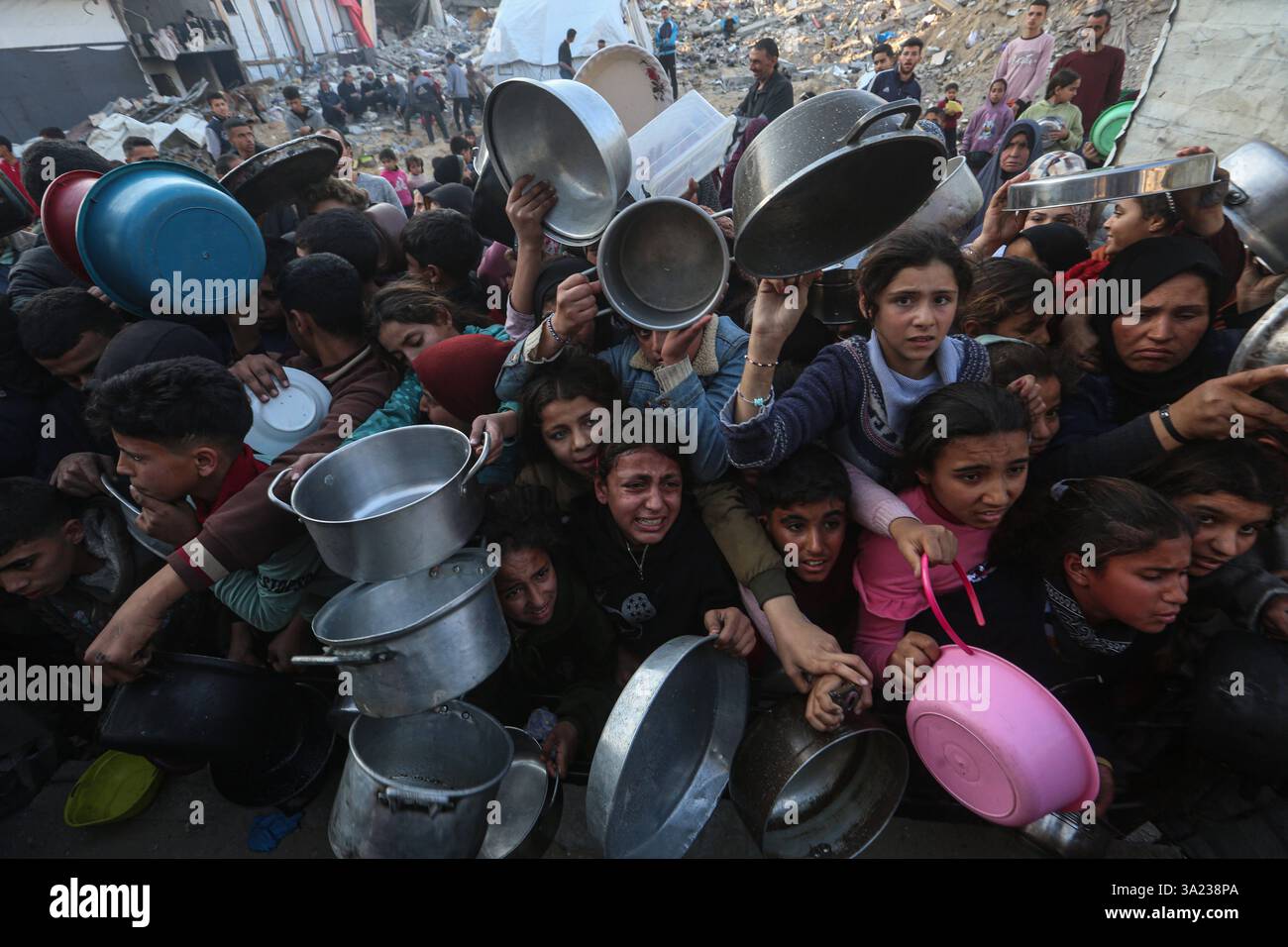 Displaced Palestinians queue to receive a share of food from a charity ...