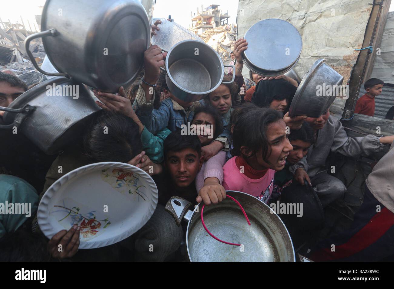 Displaced Palestinians queue to receive a share of food from a charity ...