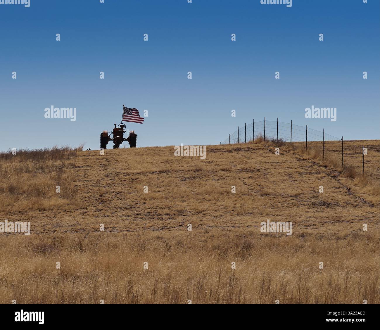 Old tractor with American flag on rural hilltop, dry grassland, blue ...