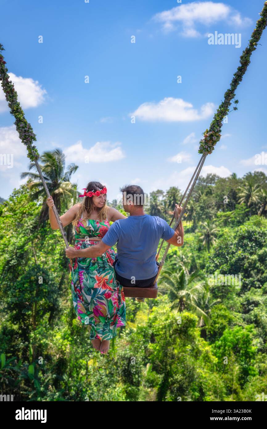 An adventurous couple joyfully swings high above vibrant green forest ...